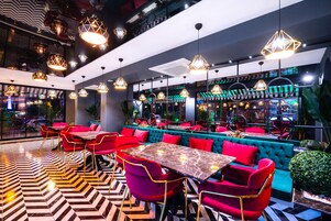 Um restaurante moderno com assentos vermelhos e azul-turquesa, luminárias pendentes geométricas e piso estampado.