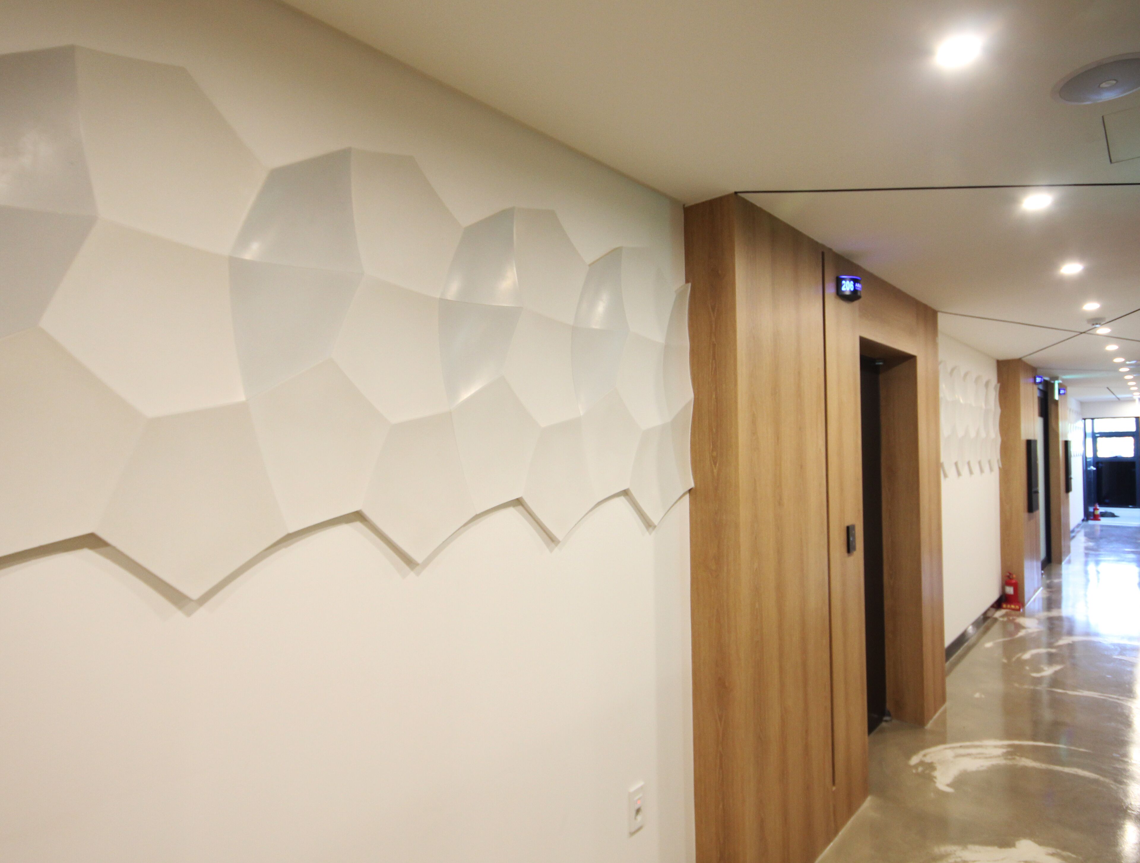 Um corredor moderno com arte geométrica na parede e uma porta de madeira.