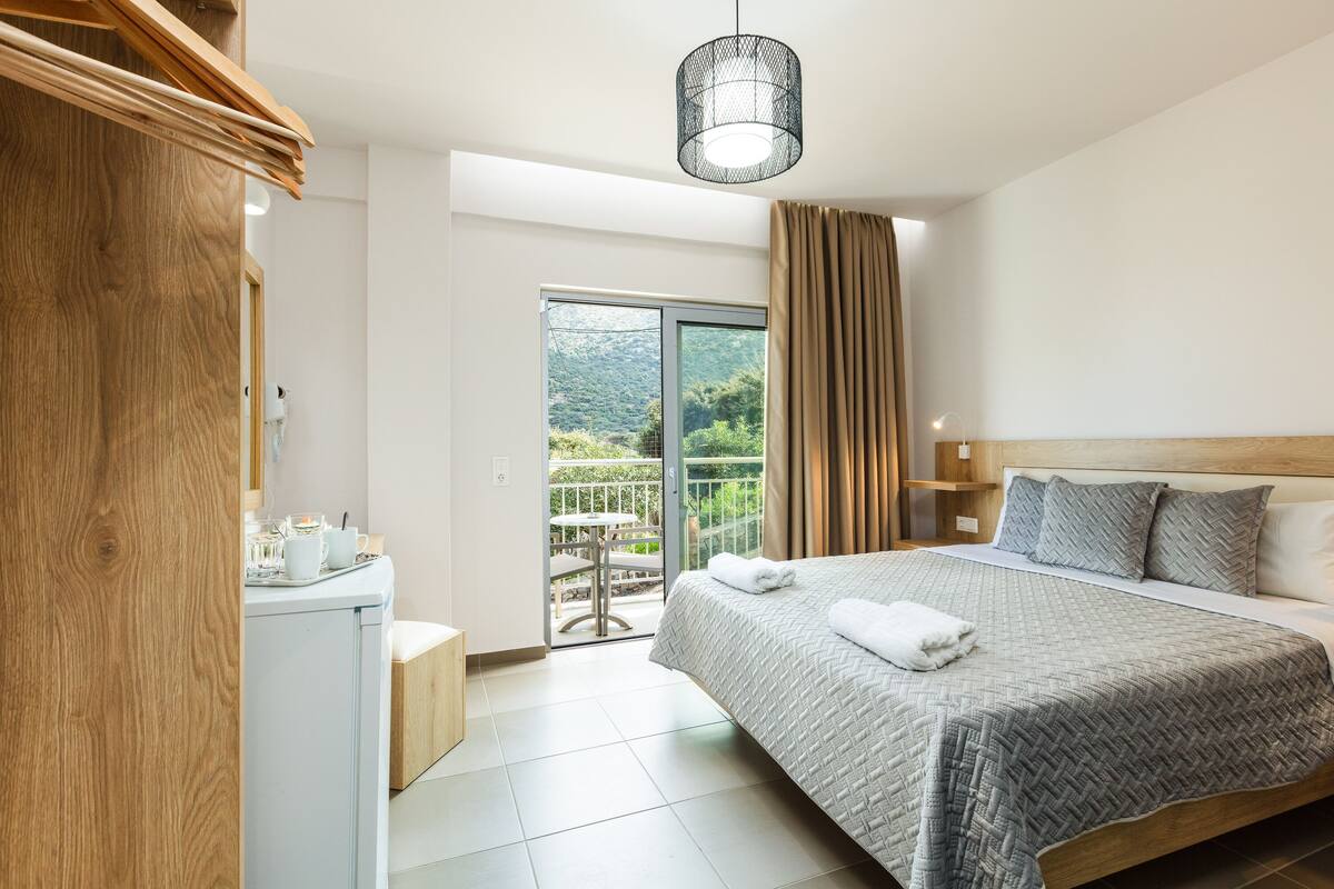 Um quarto com cama, escrivaninha, cadeira e vista para o exterior.