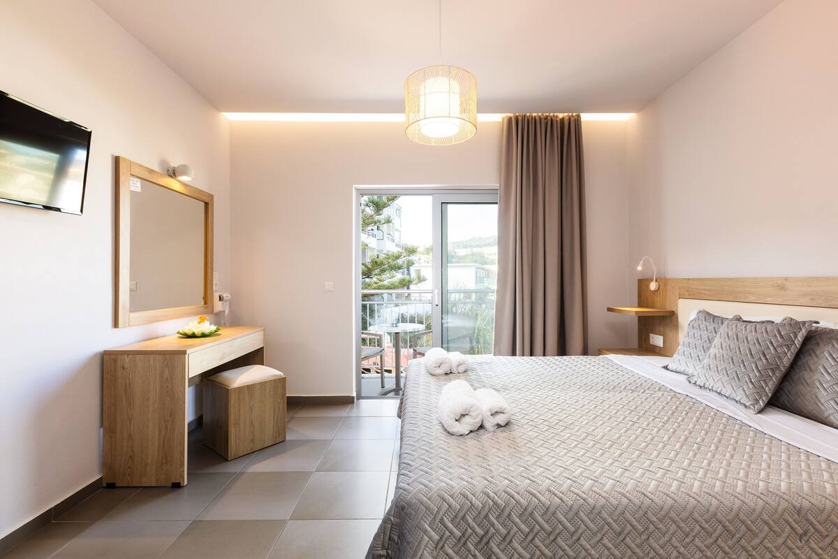 Quarto de hotel moderno com uma cama grande, uma escrivaninha de madeira, um espelho e uma varanda com vista.