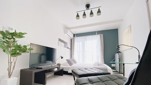 Quarto moderno com cama, mesa de cabeceira, televisão e uma grande planta em vaso.