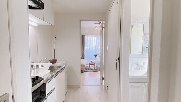 Uma cozinha moderna com armários brancos, um fogão e uma pia. Há um corredor que leva a uma sala de estar com um sofá e uma mesinha.