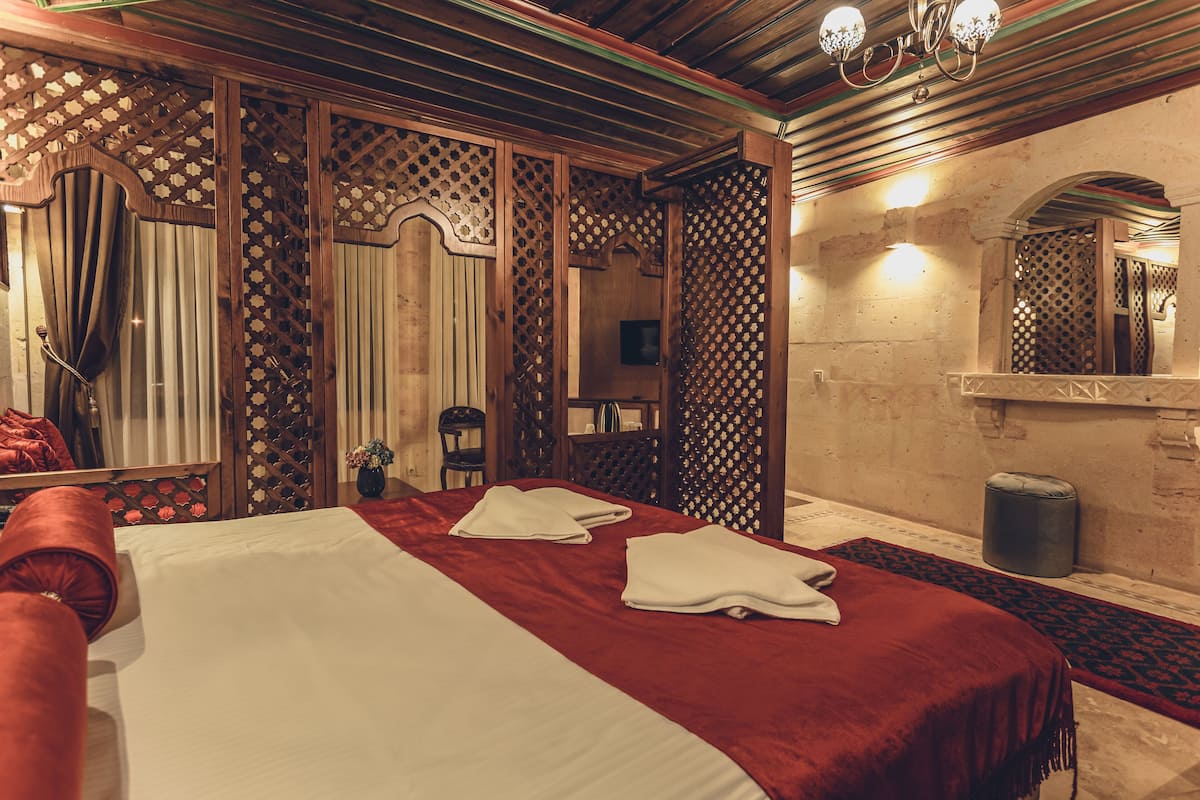 Quarto de hotel com cama grande, decoração em madeira, espelho e tapete vermelho.