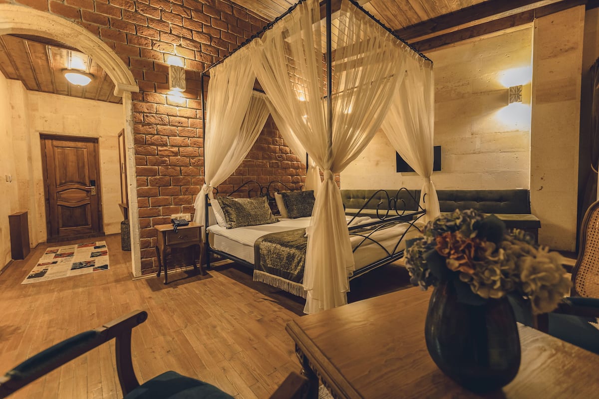 Um quarto acolhedor com parede de tijolos, cama com dossel, mesa de madeira e um vaso com flores.