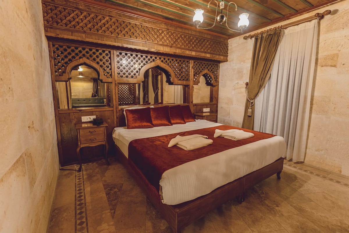Quarto tradicional com cama grande, cabeceira de madeira e espelho decorativo.