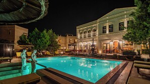 Uma área de piscina à noite, com espreguiçadeiras e uma estátua.