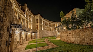 Um edifício de pedra com fachada curva, um pátio central com caminho de pedra e uma escadaria que leva a um andar superior.