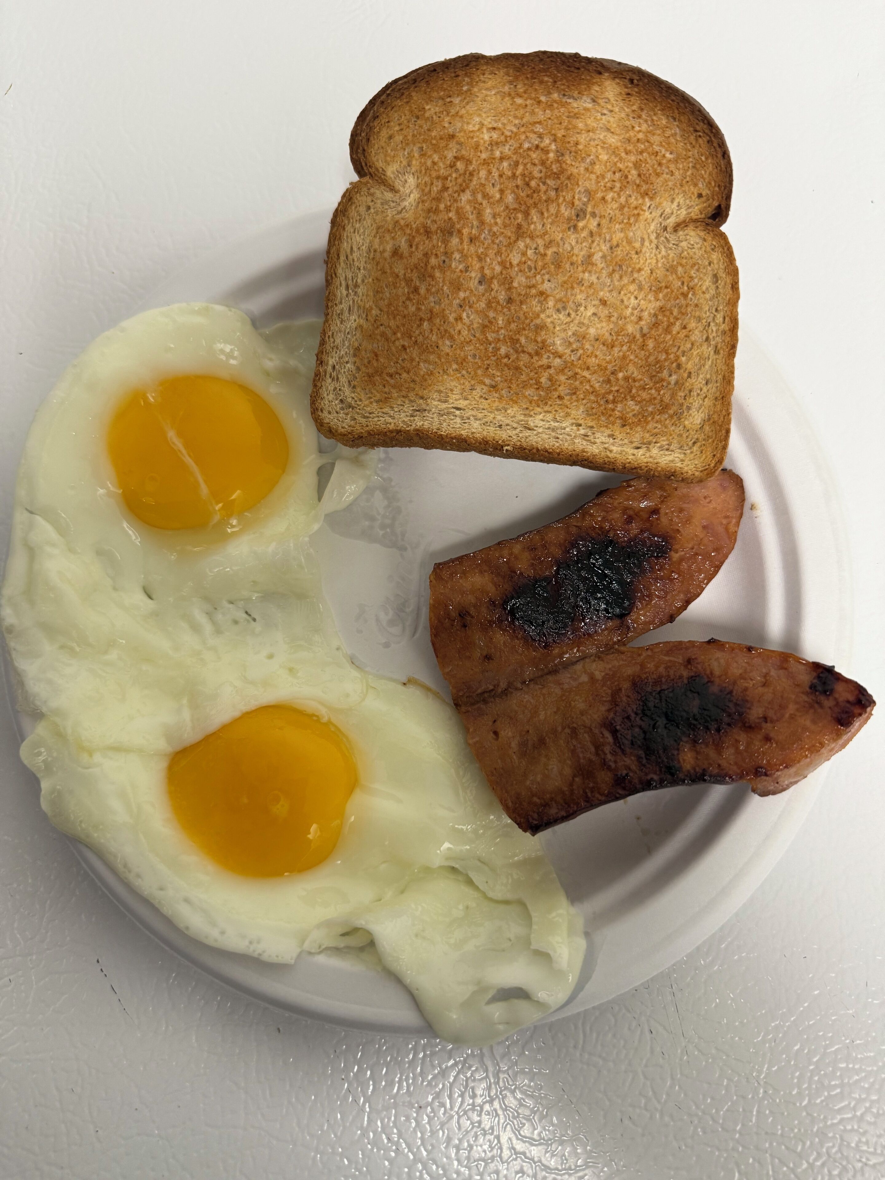 Um prato com dois ovos fritos, uma fatia de torrada e duas fatias de carne grelhada.
