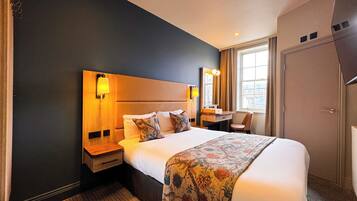 Quarto de hotel com uma cama grande, uma escrivaninha, uma cadeira e um guarda-roupa.