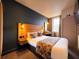 Quarto de hotel com uma cama grande, uma escrivaninha, uma cadeira e um guarda-roupa.