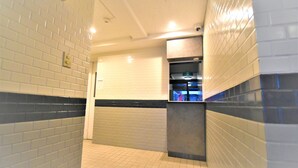 Um corredor com paredes e chão revestidos de azulejos brancos e pretos, e uma porta fechada.