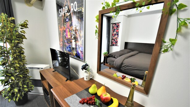 Quarto de hotel com cama, televisão, escrivaninha com planta, cesta de frutas e espelho.