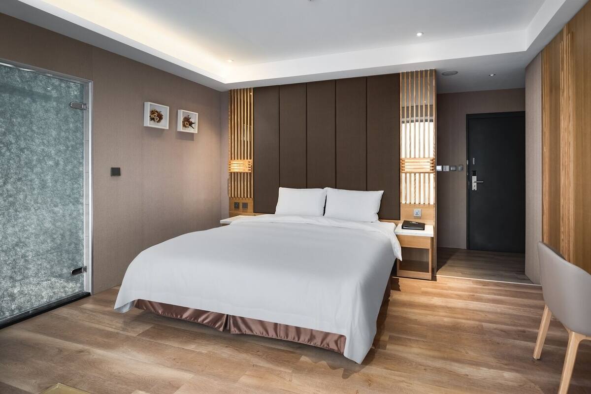 Quarto moderno com cama grande, painéis de madeira, mesa de cabeceira e uma cadeira.