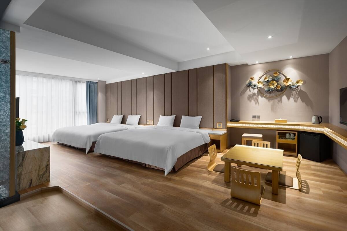 Quarto de hotel moderno com duas camas, área de refeições e televisão.
