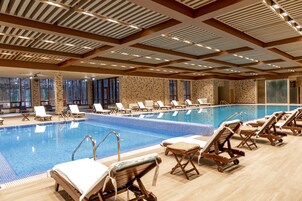 Uma grande piscina interior com várias espreguiçadeiras e um painel de parede de pedra.