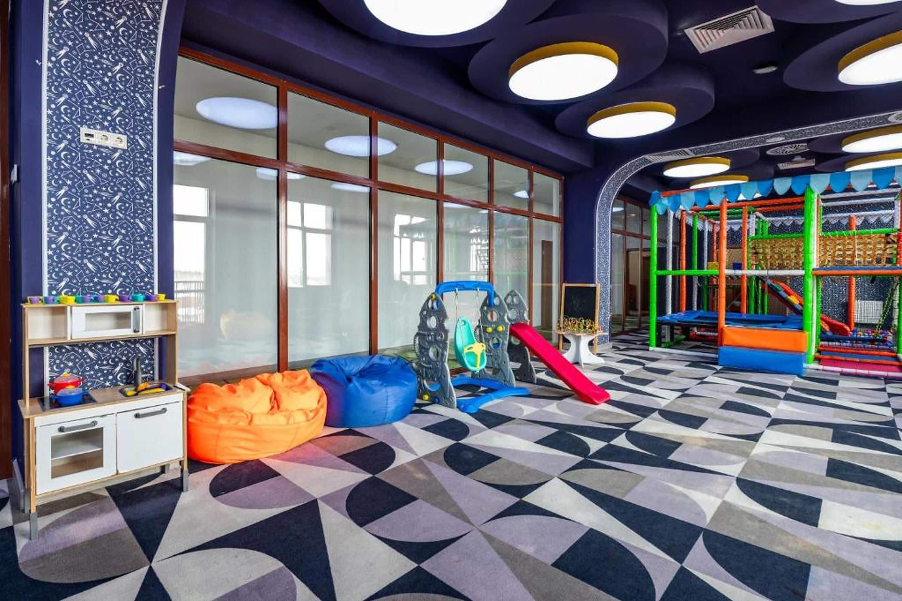 Uma área de recreação infantil com piso estampado em padrões geométricos, um escorregador e uma estrutura de escalada.