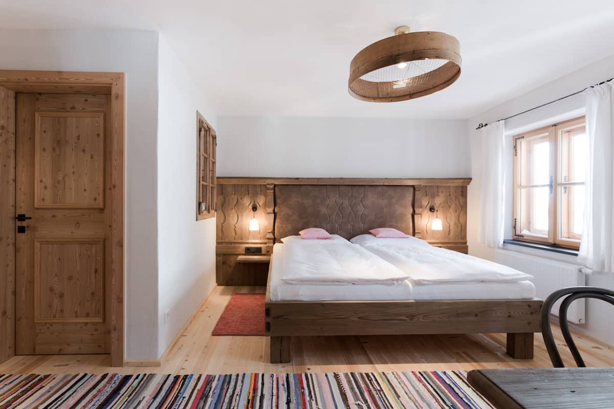 Quarto com cama de madeira, tapete vermelho, porta de madeira e janela com cortinas.
