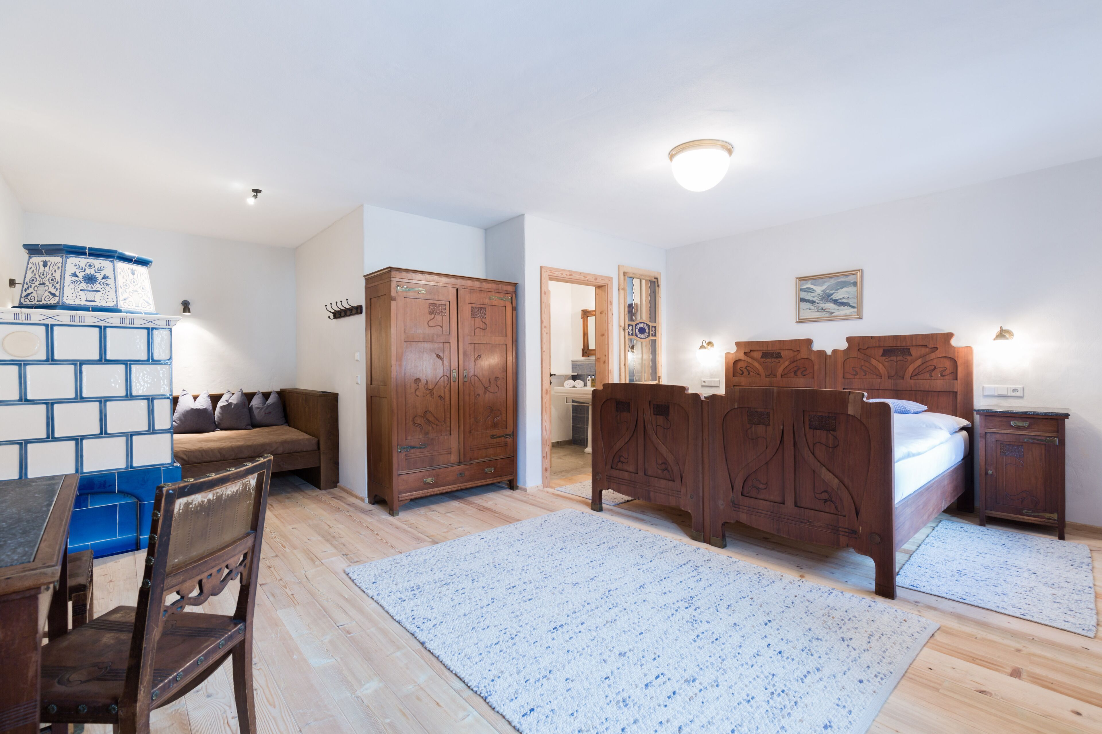 Quarto com cama de madeira, guarda-roupa de madeira, armário de madeira, um banco com azulejos azuis e brancos e um tapete branco.