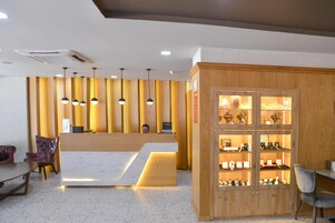 Uma área de recepção com balcão de madeira, espaço de espera com cadeiras, iluminação pendente e um expositor com objetos.