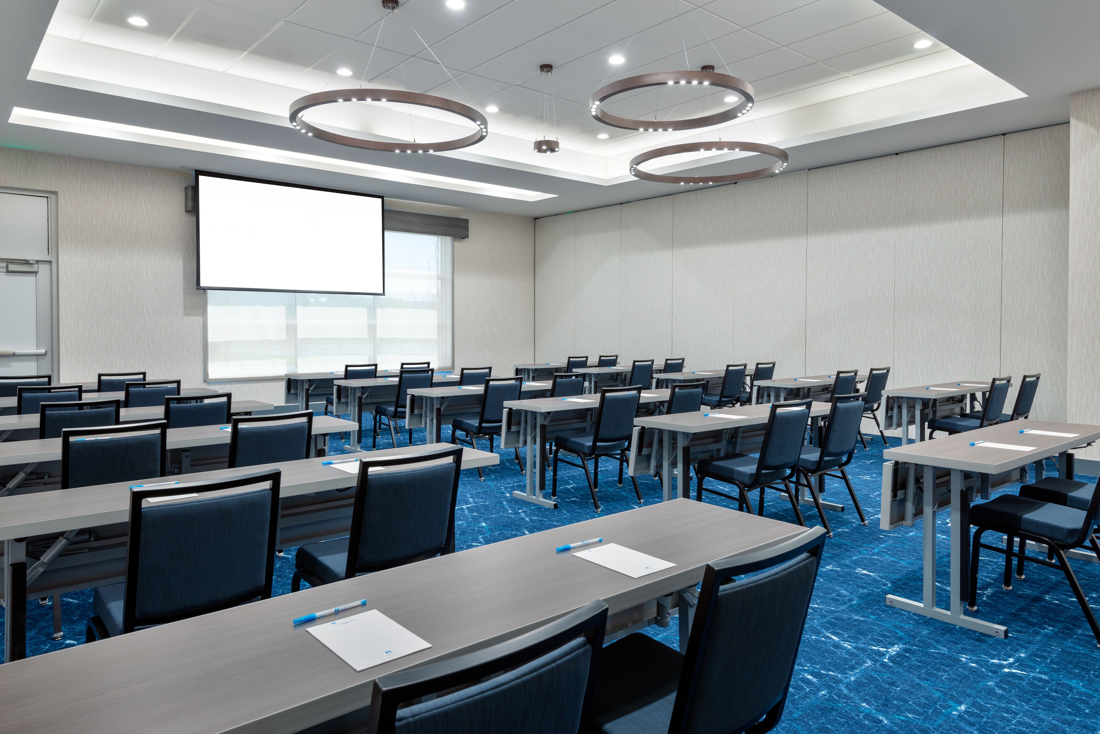 Uma sala de conferências com várias mesas e cadeiras, uma tela grande e um projetor.