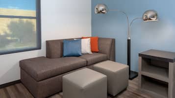 Uma sala de estar moderna com um sofá, pufes, uma mesa lateral e um abajur.