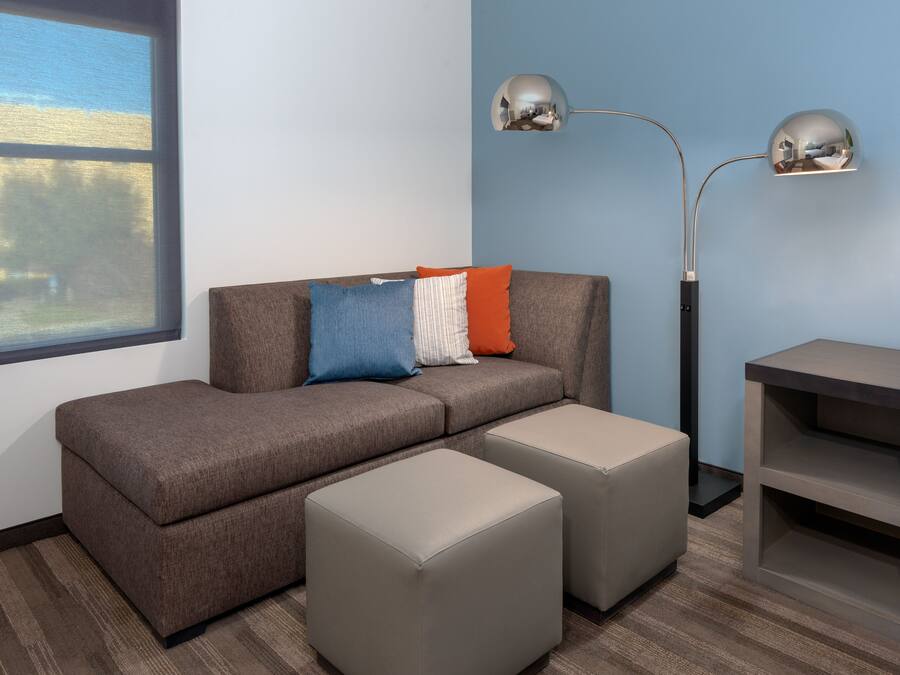 Uma sala de estar moderna com um sofá, pufes, uma mesa lateral e um abajur.