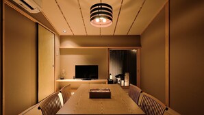 Uma sala de conferências com uma longa mesa de madeira, cadeiras, uma televisão e um lustre.