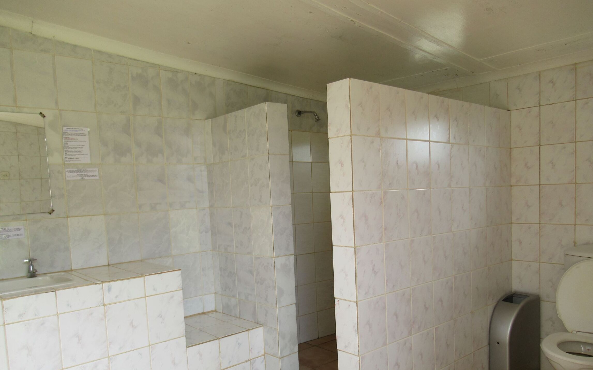 Casa de banho com azulejos brancos, zona de duche e sanita.
