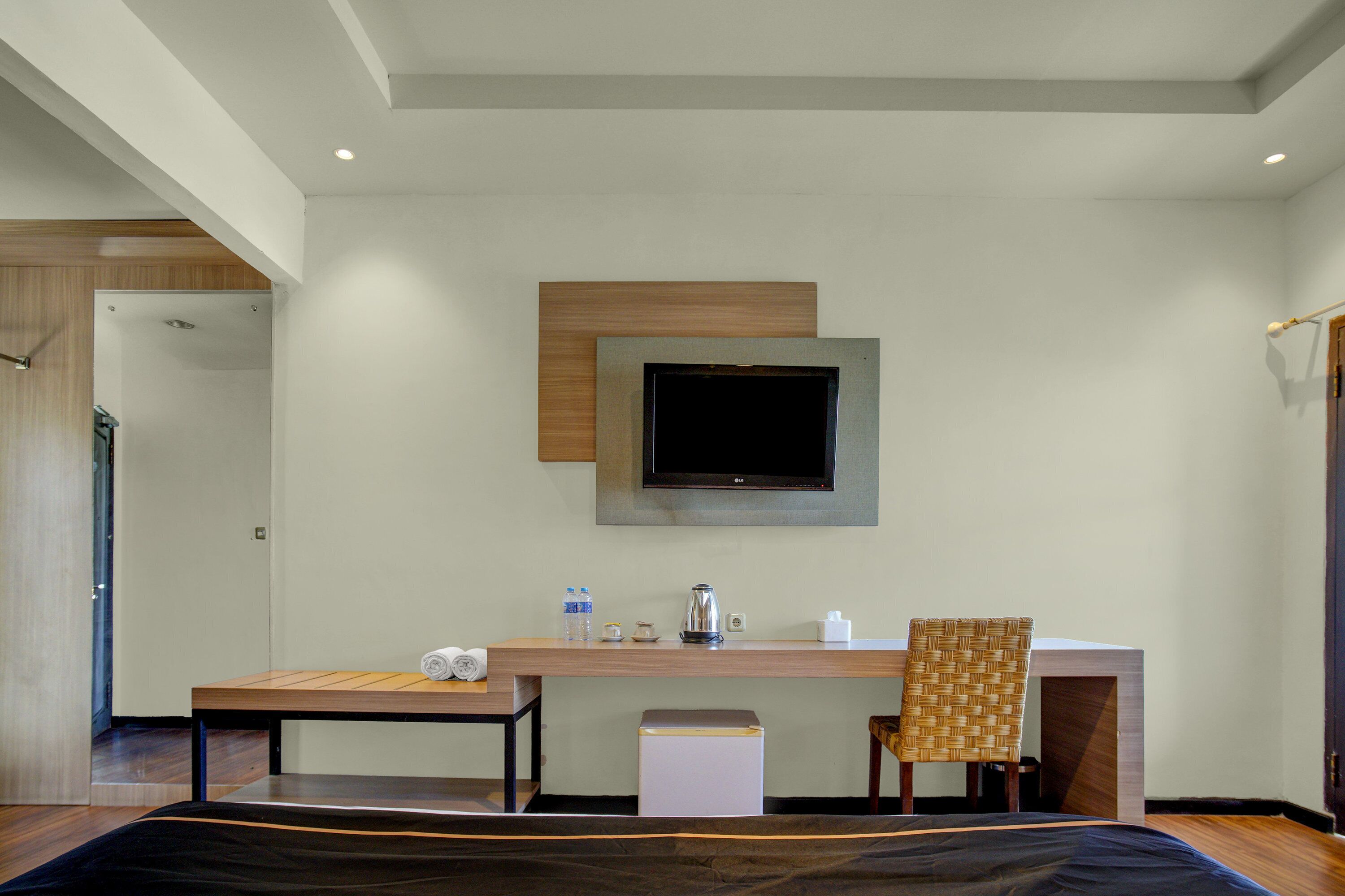 Quarto de hotel com cama, escrivaninha, cadeira, televisão e um pequeno cesto de lixo.