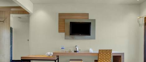 Quarto de hotel com cama, escrivaninha, cadeira, televisão e um pequeno cesto de lixo.