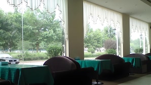 Um restaurante com mesas cobertas por toalhas verdes, cadeiras e vista para árvores e um carro na rua.
