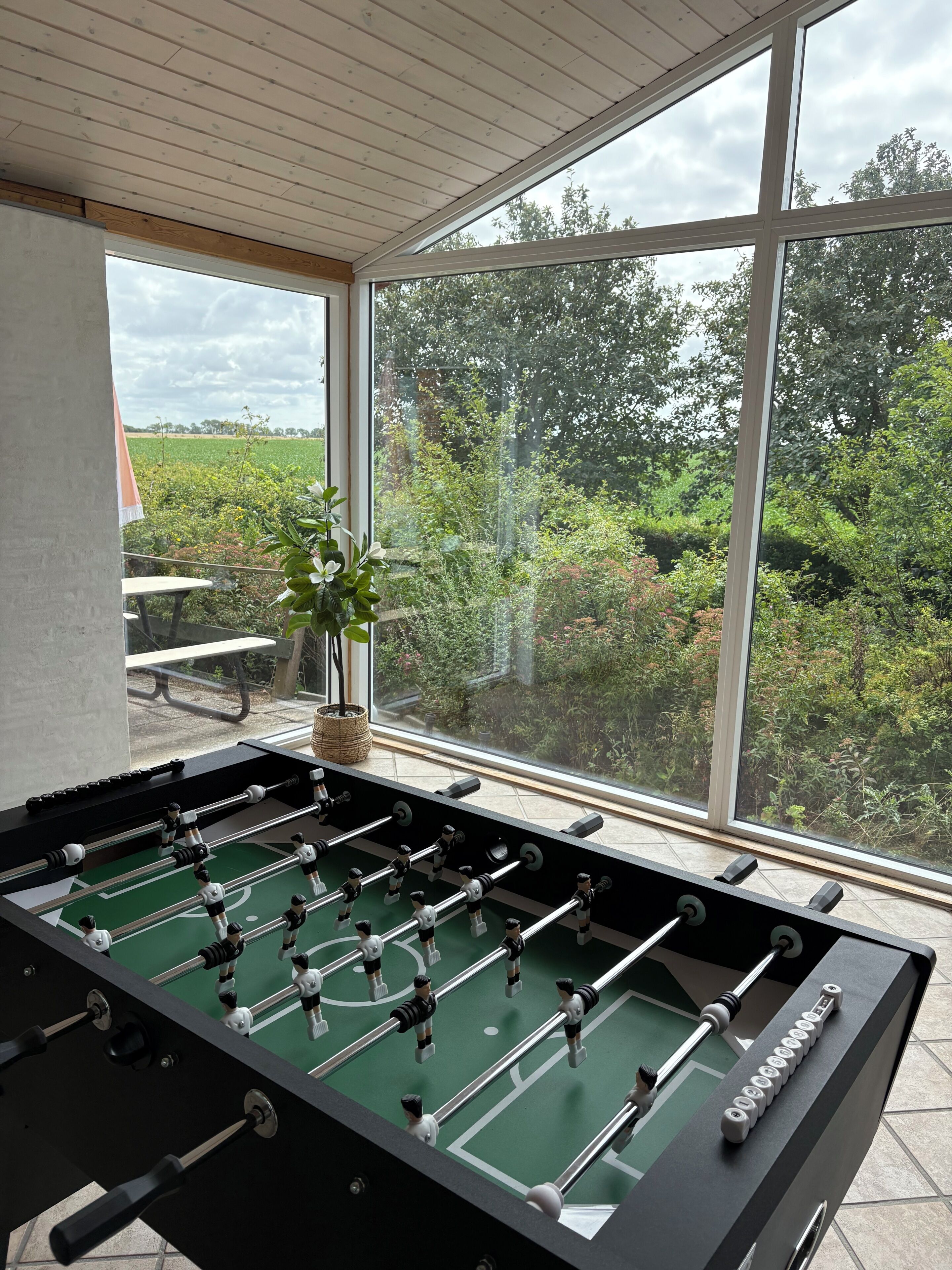 Uma mesa de pebolim em um quarto com grandes janelas com vista para um jardim.