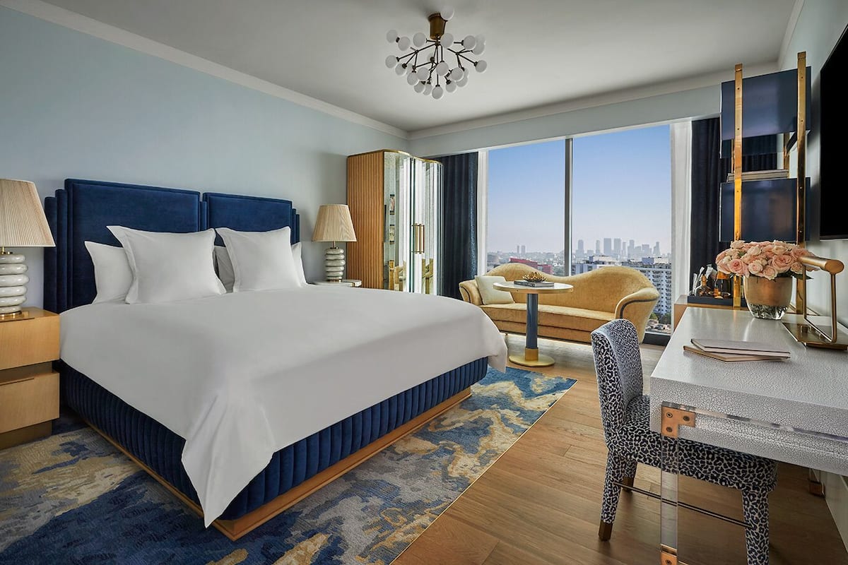 Quarto de hotel moderno com uma cama grande, um sofá, uma escrivaninha e vista para a cidade.