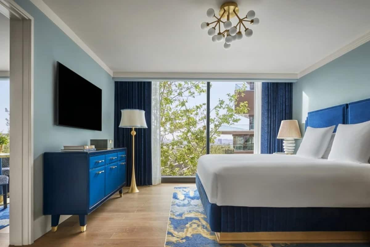 Quarto de hotel com uma cama grande, televisão de tela plana, cômoda azul e vista para o exterior.