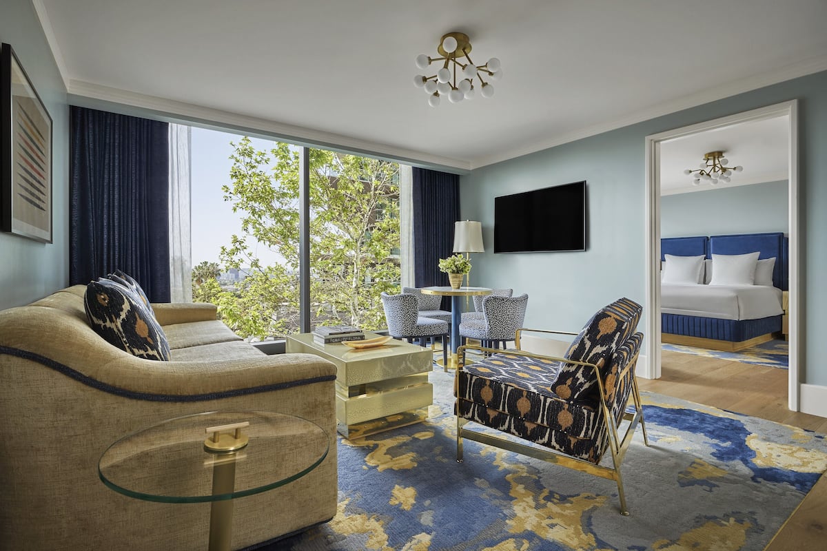 Quarto de hotel moderno com uma janela grande, um sofá, uma mesa de jantar e uma cama.