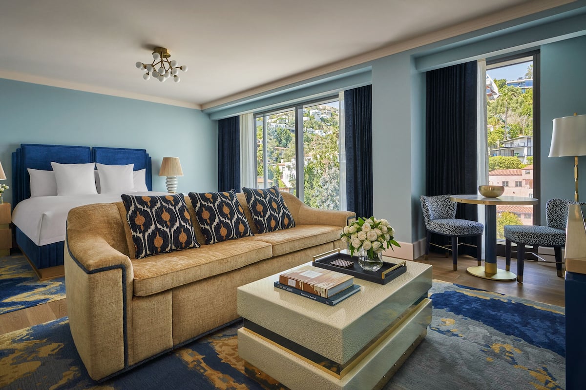 Quarto de hotel com uma cama grande, um sofá, uma mesa de centro e vista para a cidade.