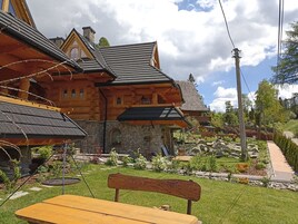 Uma cabana de toras com base de pedra, um deck de madeira e um jardim com um banco.