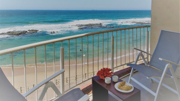 Uma varanda com vista para o oceano, uma mesa com um prato de comida e duas cadeiras.