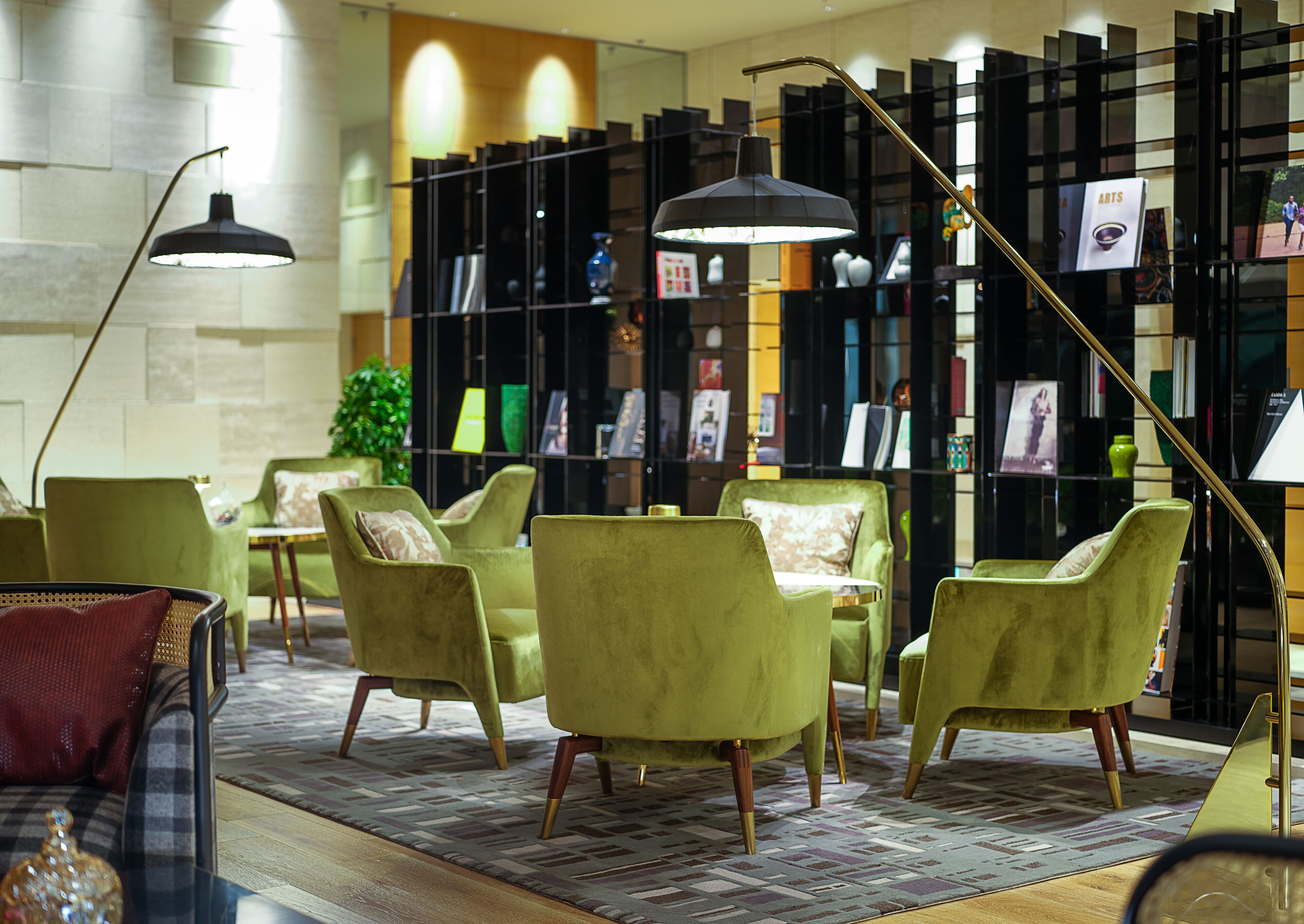 Um hall com poltronas verdes, um tapete estampado e uma luminária pendente preta.