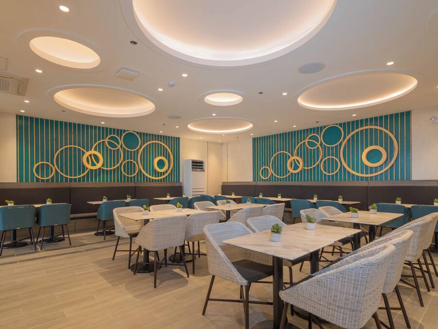 Um restaurante moderno com mesas redondas e cadeiras azuis, com um design de parede em tons de verde-água e dourado.