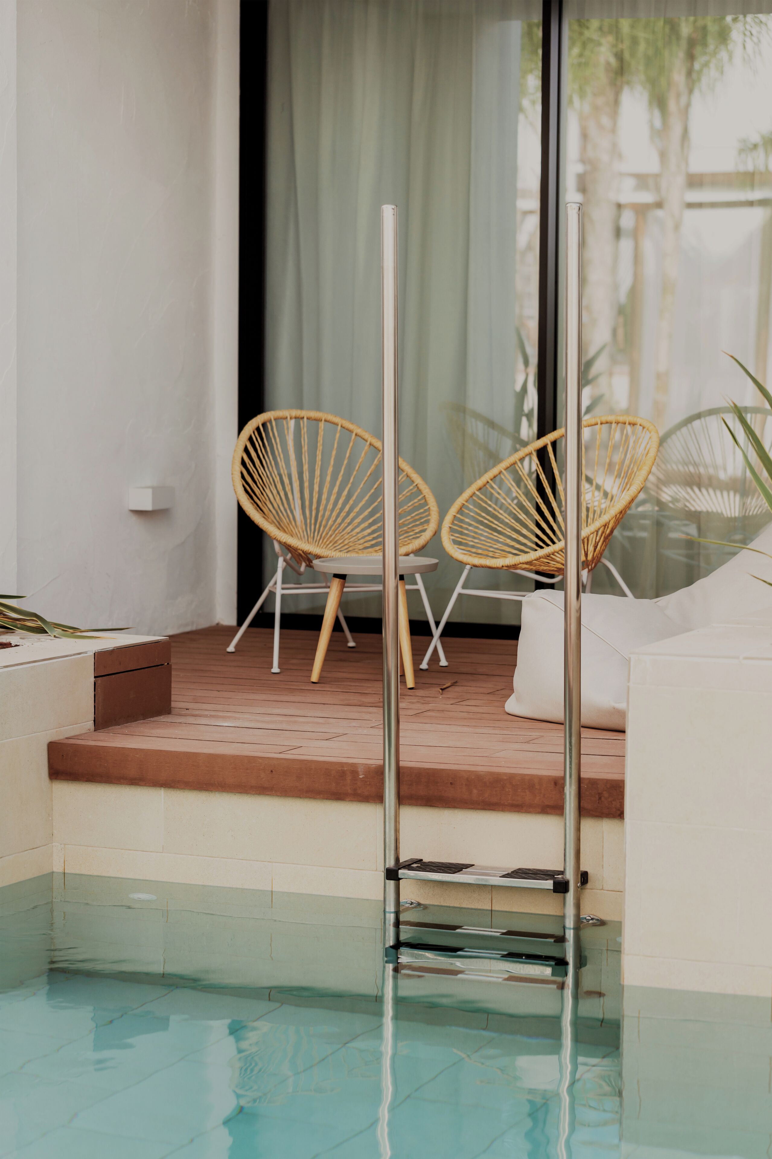 Área da piscina com duas cadeiras de vime, um sofá branco e uma porta de vidro que dá para uma varanda.
