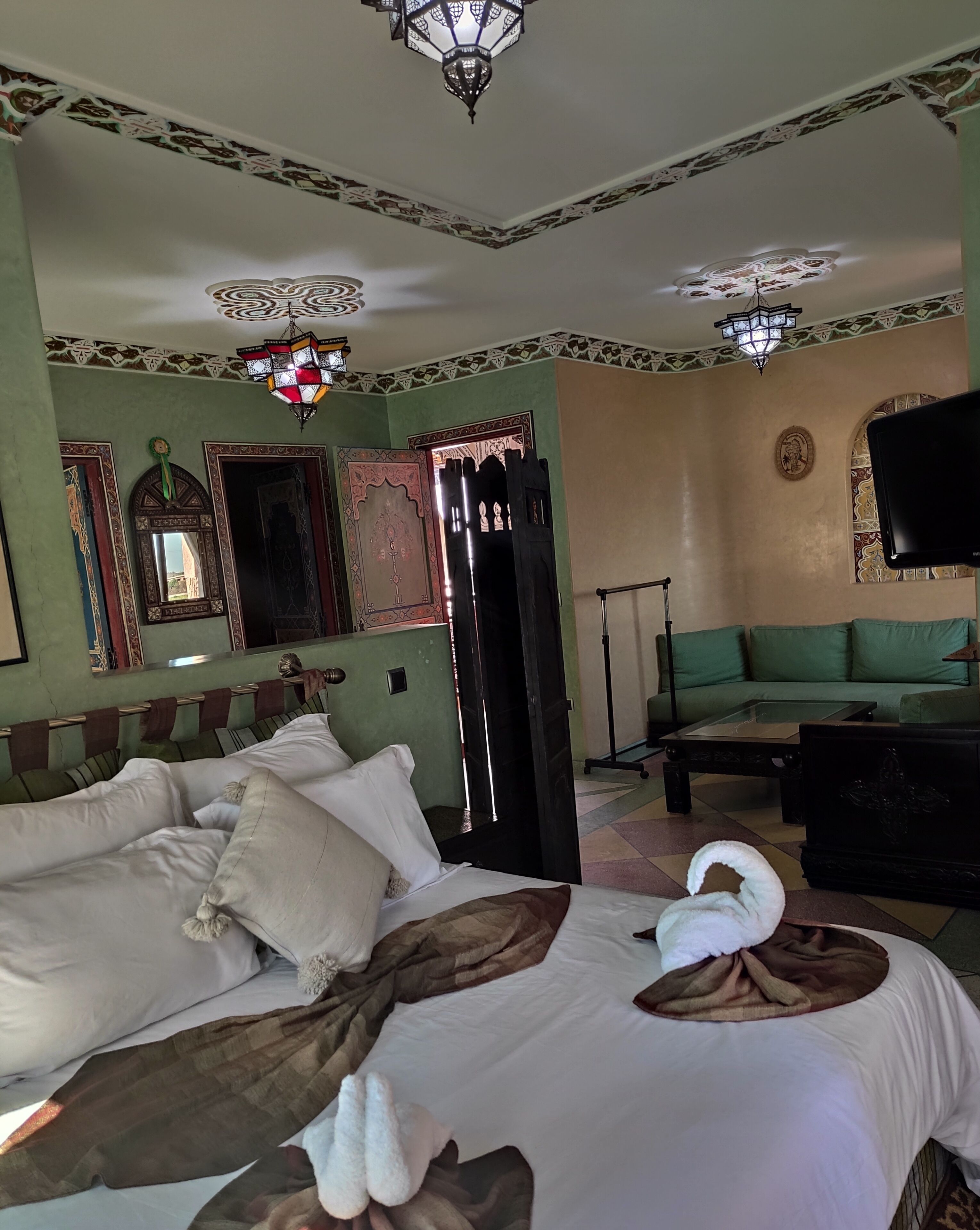 Quarto de hotel com uma cama, um sofá verde, uma televisão e painéis decorativos na parede.