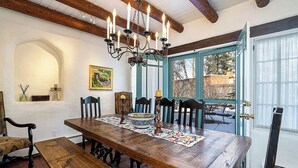 Uma área de refeições com mesa de madeira, bancos e cadeiras. Há um candelabro sobre a mesa e uma janela com vista para o exterior.