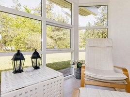 Quarto com janelas amplas, uma cadeira branca e duas lanternas pretas sobre uma mesa branca.
