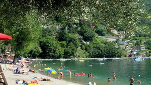 Uma praia com pessoas nadando e tomando sol, cercada por árvores e casas.