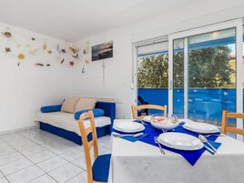 Quarto com uma mesa de jantar posta para quatro pessoas, um sofá com almofadas azuis e uma parede decorada com diversos objetos.