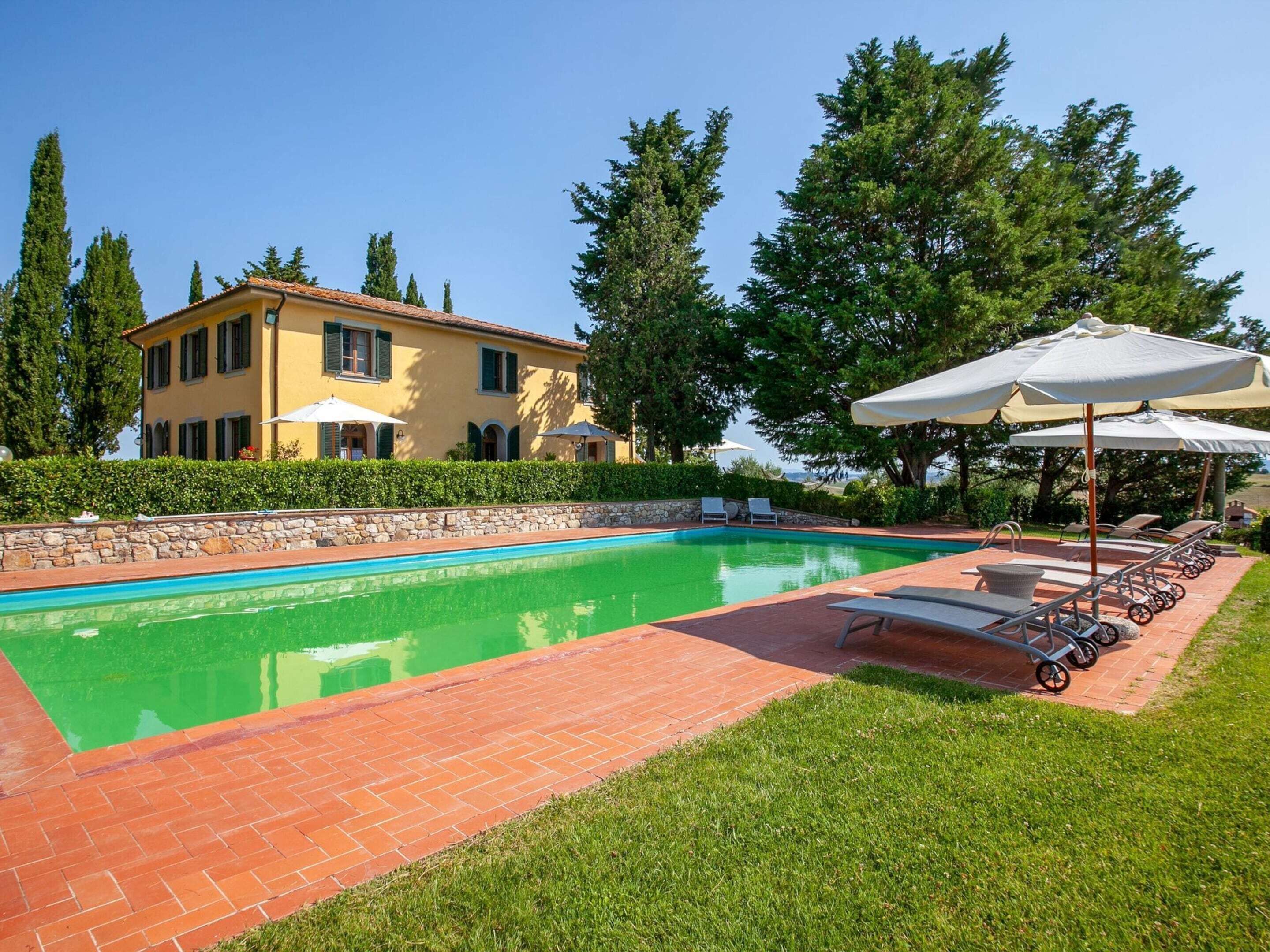 Uma área de piscina com um terraço de tijolos, espreguiçadeiras e guarda-sóis.
