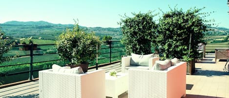 Terraço com mobiliário de vime e plantas em vasos, com vista para uma paisagem deslumbrante.