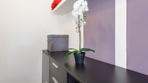 Quarto moderno com escrivaninha de madeira escura, uma orquídea em vaso e uma toalha vermelha numa prateleira branca.