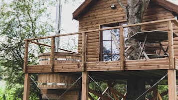 Uma casa na árvore de madeira com varanda e um nível inferior, rodeada por árvores.